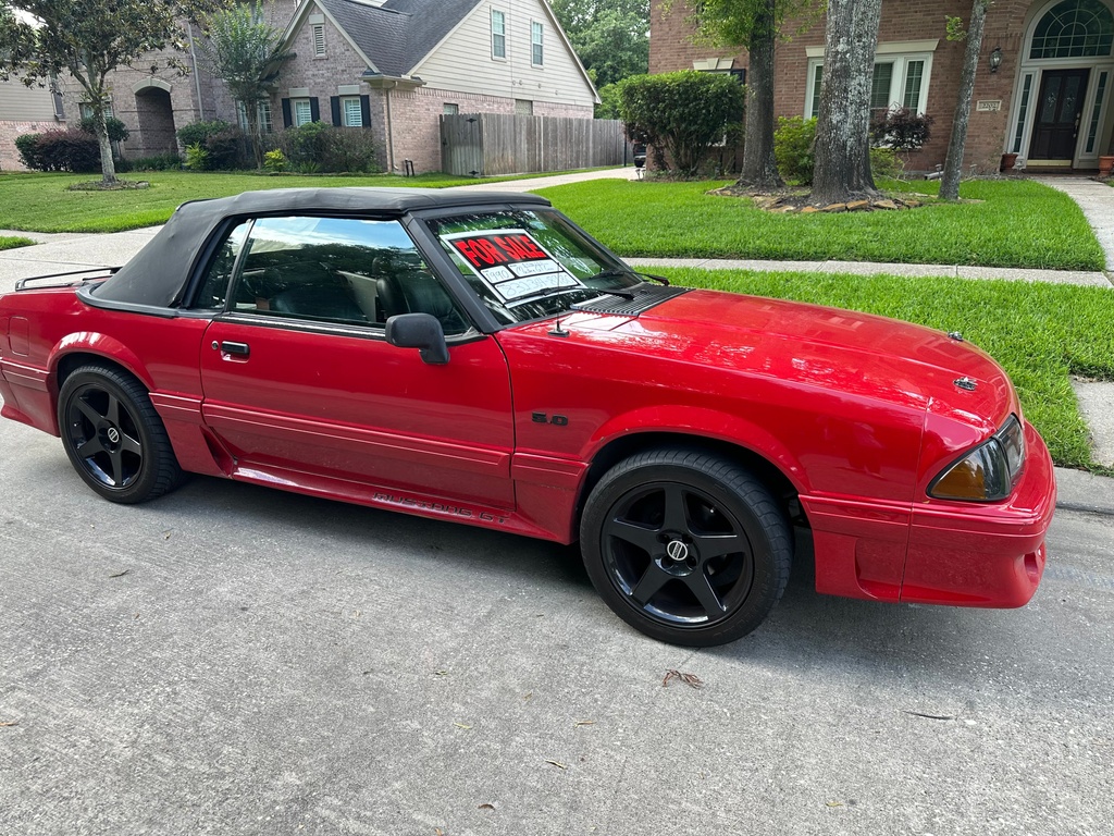 Red 1990 fox body mustang with black wheels driving...